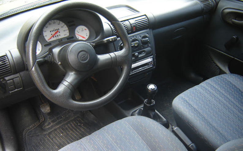 Foto mostrando a cabine do carro. É possível ver o colante, o câmbio, o ...