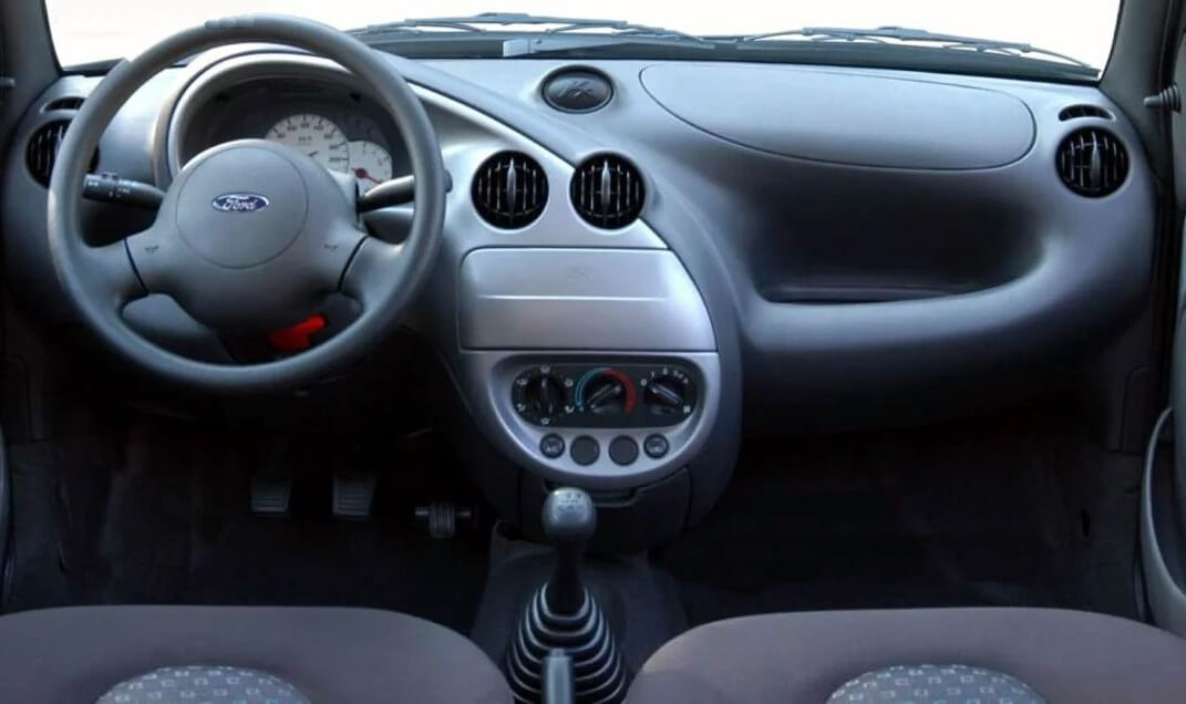 Foto mostrando a cabine do carro. É possível ver o volante, o painel, o câmbio e os assentos dos ...