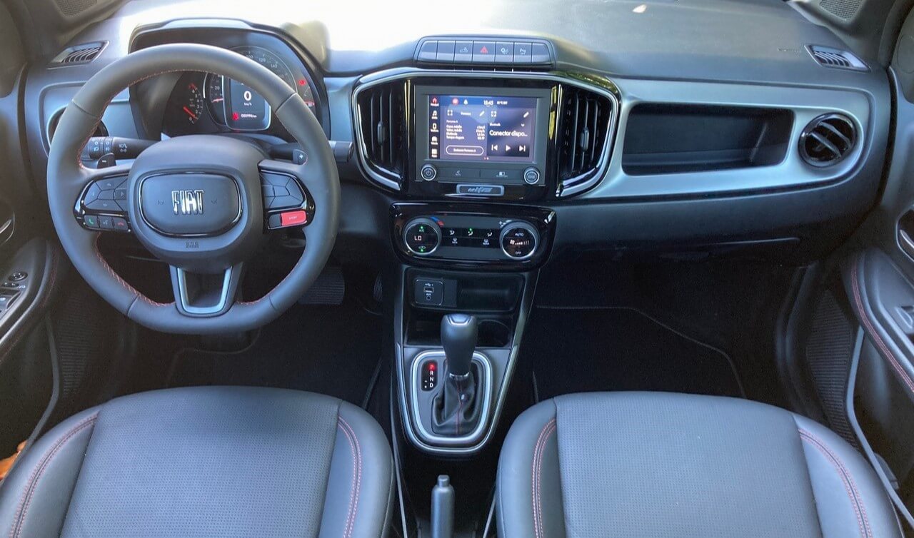 Foto mostrando a cabine do carro. É possível ver o painel, o console ...