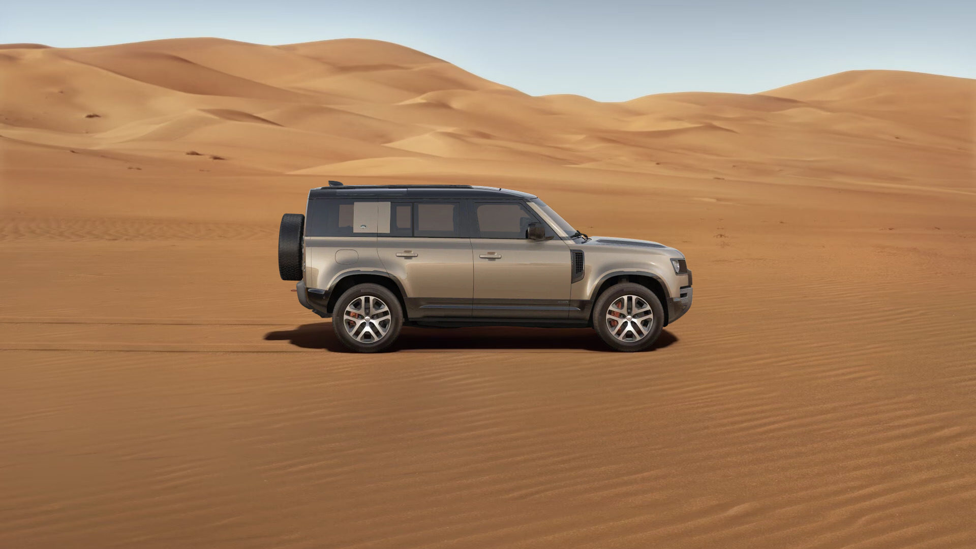 Foto da lateral do Land Rover Defender 110 PHEV no deserto, exibindo ...