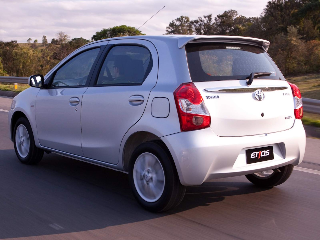 A imagem mostra um Toytota Etios na cor prateada circulando em uma estrada.